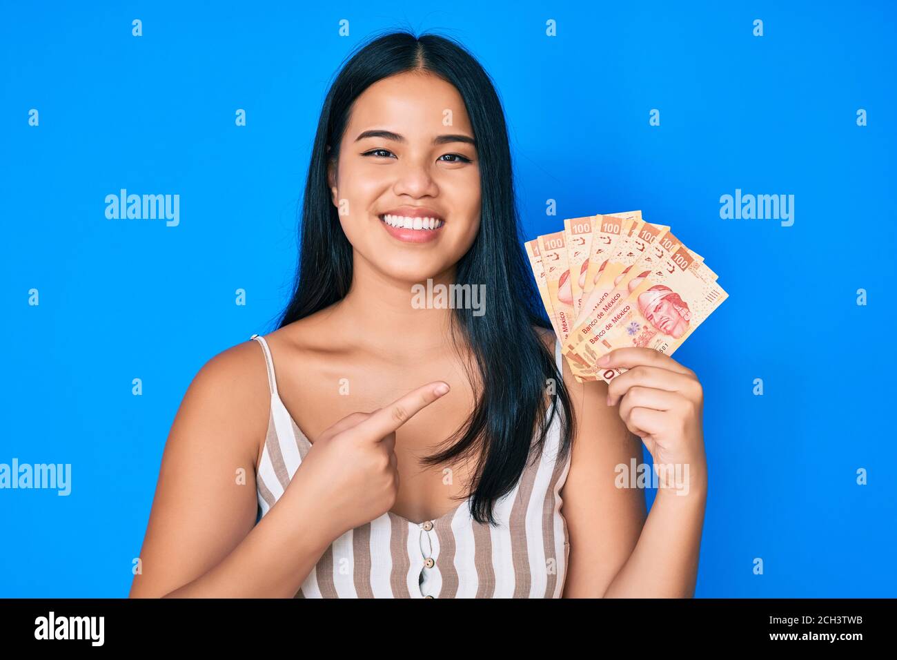 Young beautiful asian girl holding mexican pesos smiling happy pointing ...