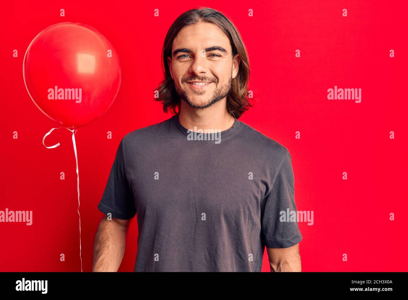 Young handsome man holding balloon looking positive and happy standing and smiling with a ...