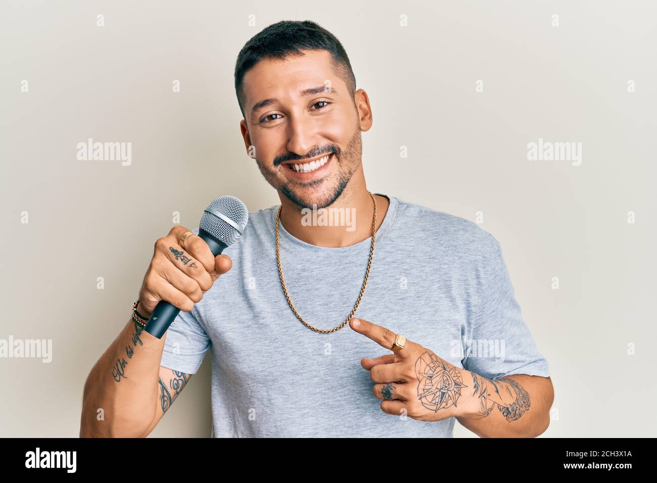 Handsome man with tattoos singing song using microphone smiling happy ...