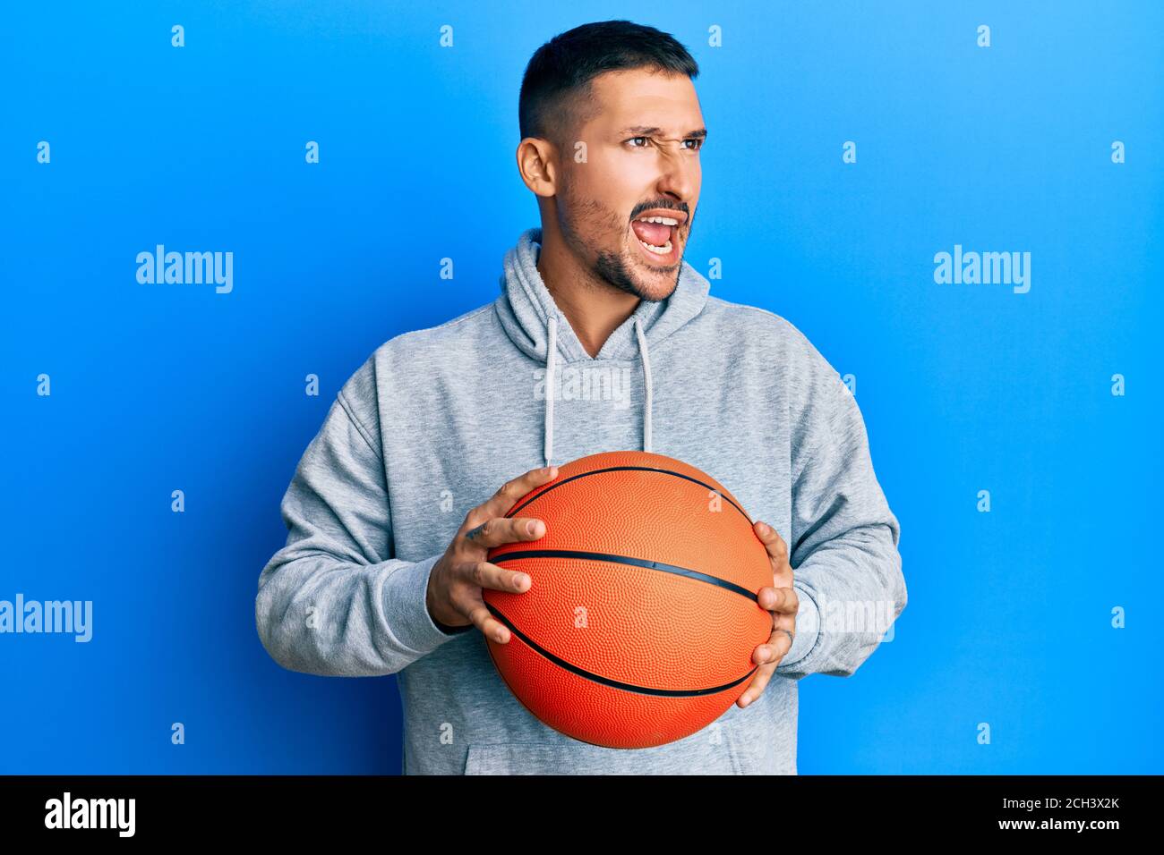 Handsome man with tattoos holding basketball ball angry and mad ...