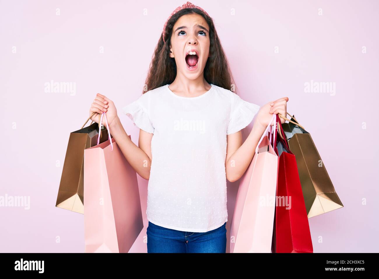 Cute hispanic girl holding shopping bags angry and mad screaming ...