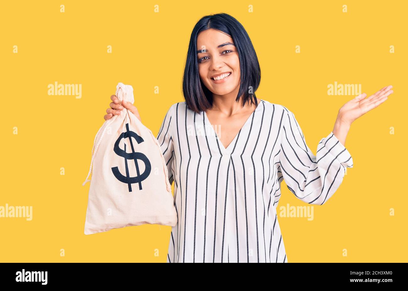 Young beautiful latin woman holding money bag with dollar symbol ...