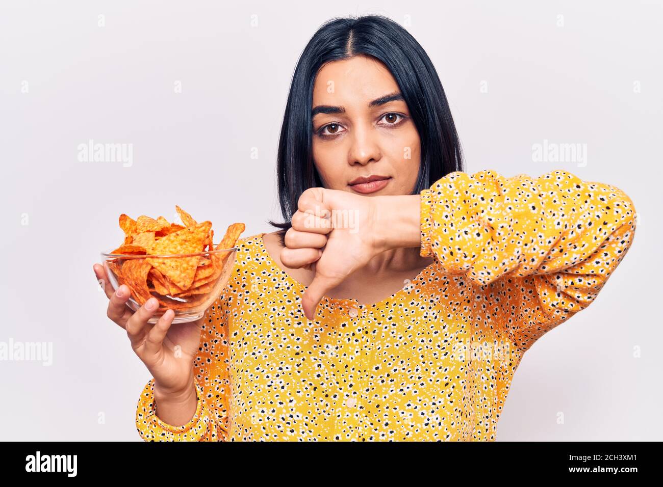 Young beautiful latin woman holding nachos potato chips with angry face ...