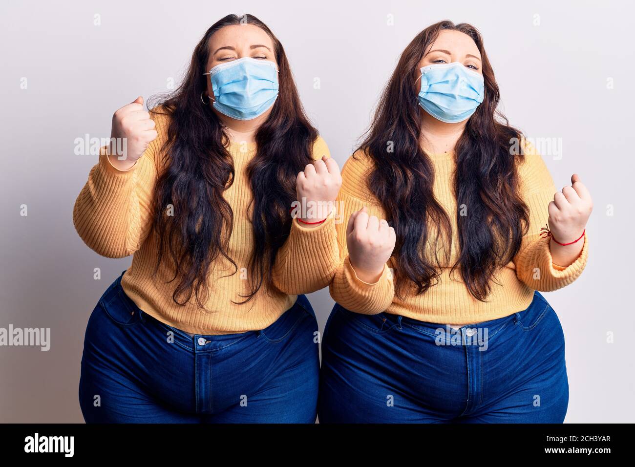 Young plus size twins wearing medical mask very happy and excited doing ...