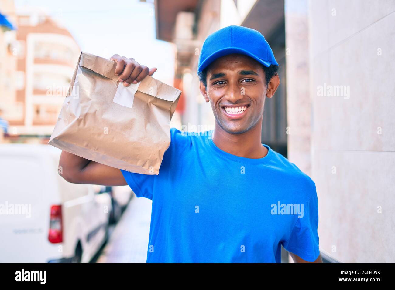 African delivery man wearing courier uniform outdoors holding take away ...