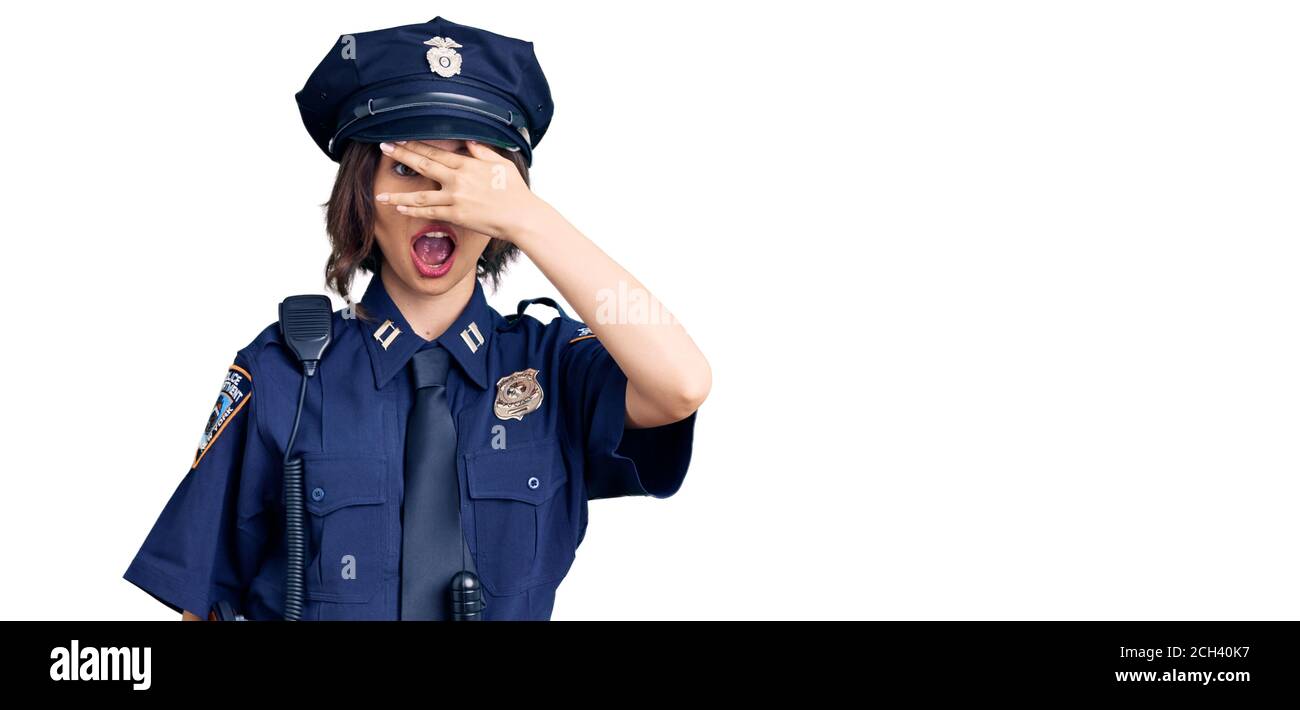 Young beautiful girl wearing police uniform peeking in shock covering ...