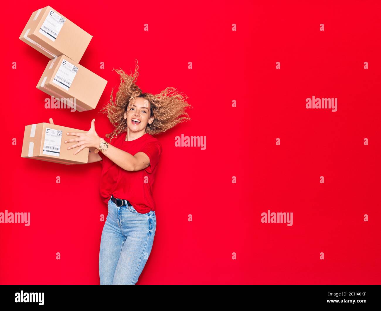 Young beautiful curly deliverywoman holding package smiling happy ...