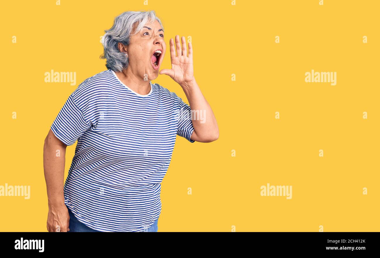 Senior woman with gray hair wearing casual striped clothes shouting and ...