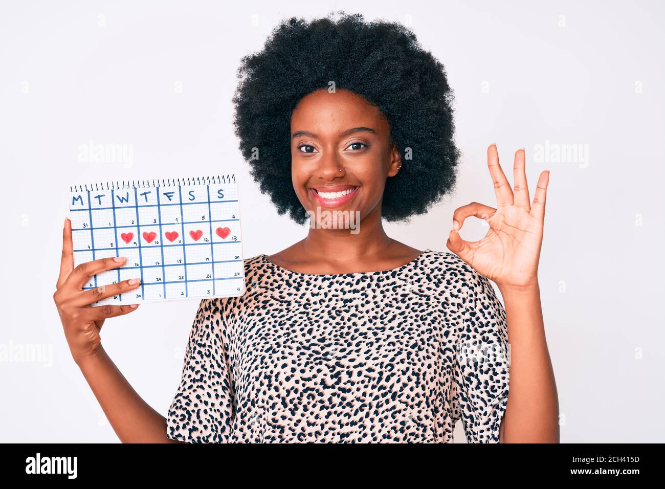 Young african american woman holding heart calendar doing ok sign with ...