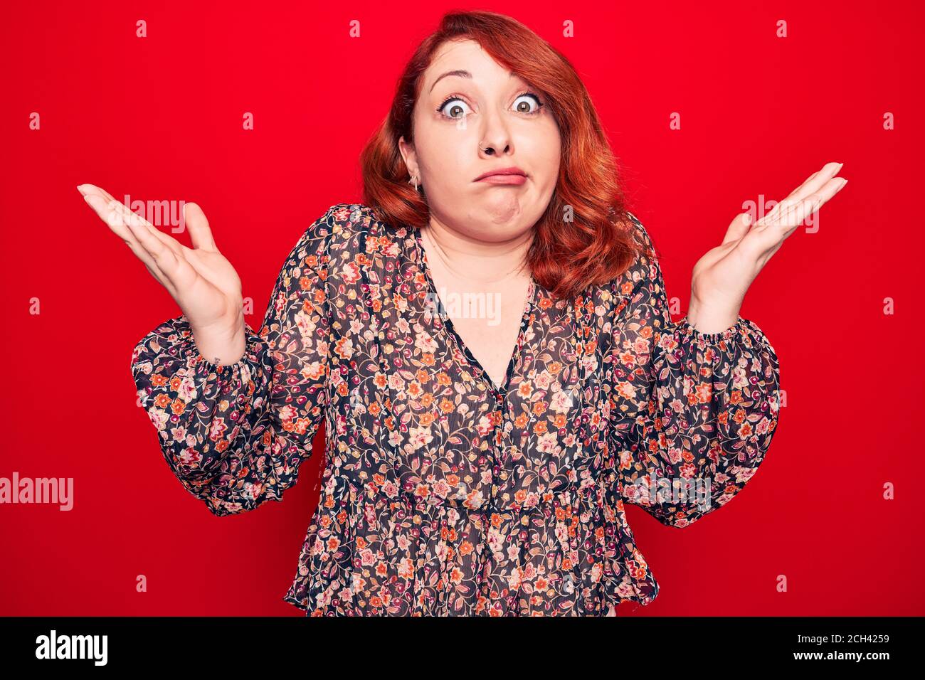 Young beautiful redhead woman wearing floral casual dress standing over ...
