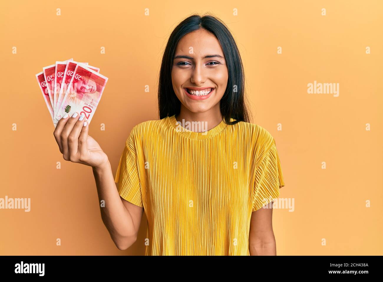 Young brunette woman holding 20 israel shekels banknotes looking ...