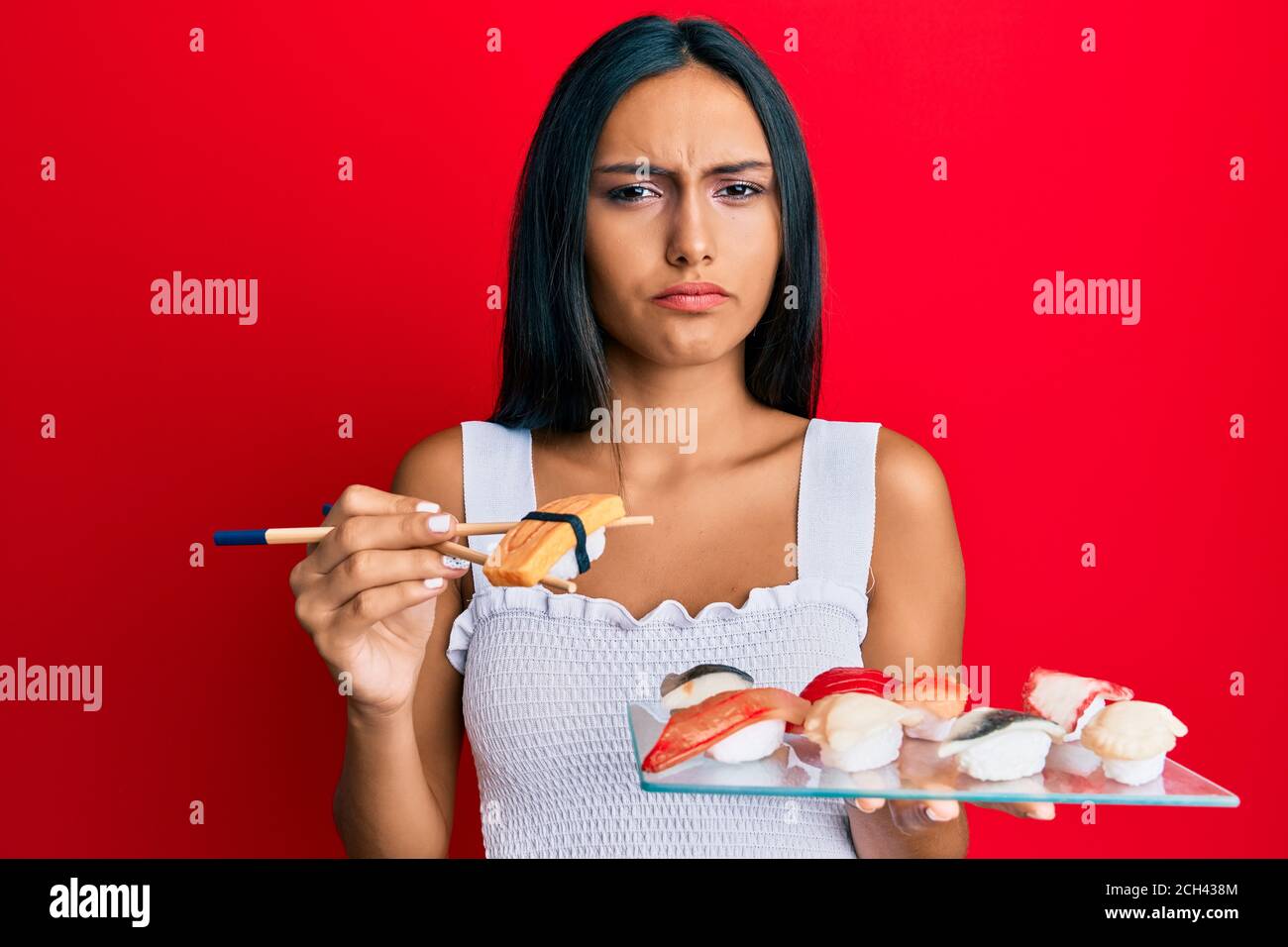 Young brunette woman eating omelet sushi using chopsticks skeptic and ...