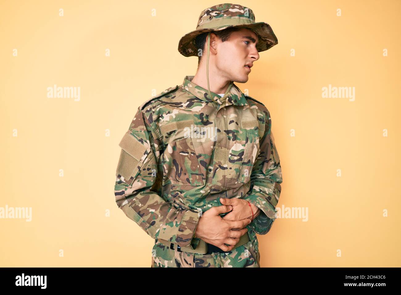 Young handsome man wearing camouflage army uniform with hand on stomach ...