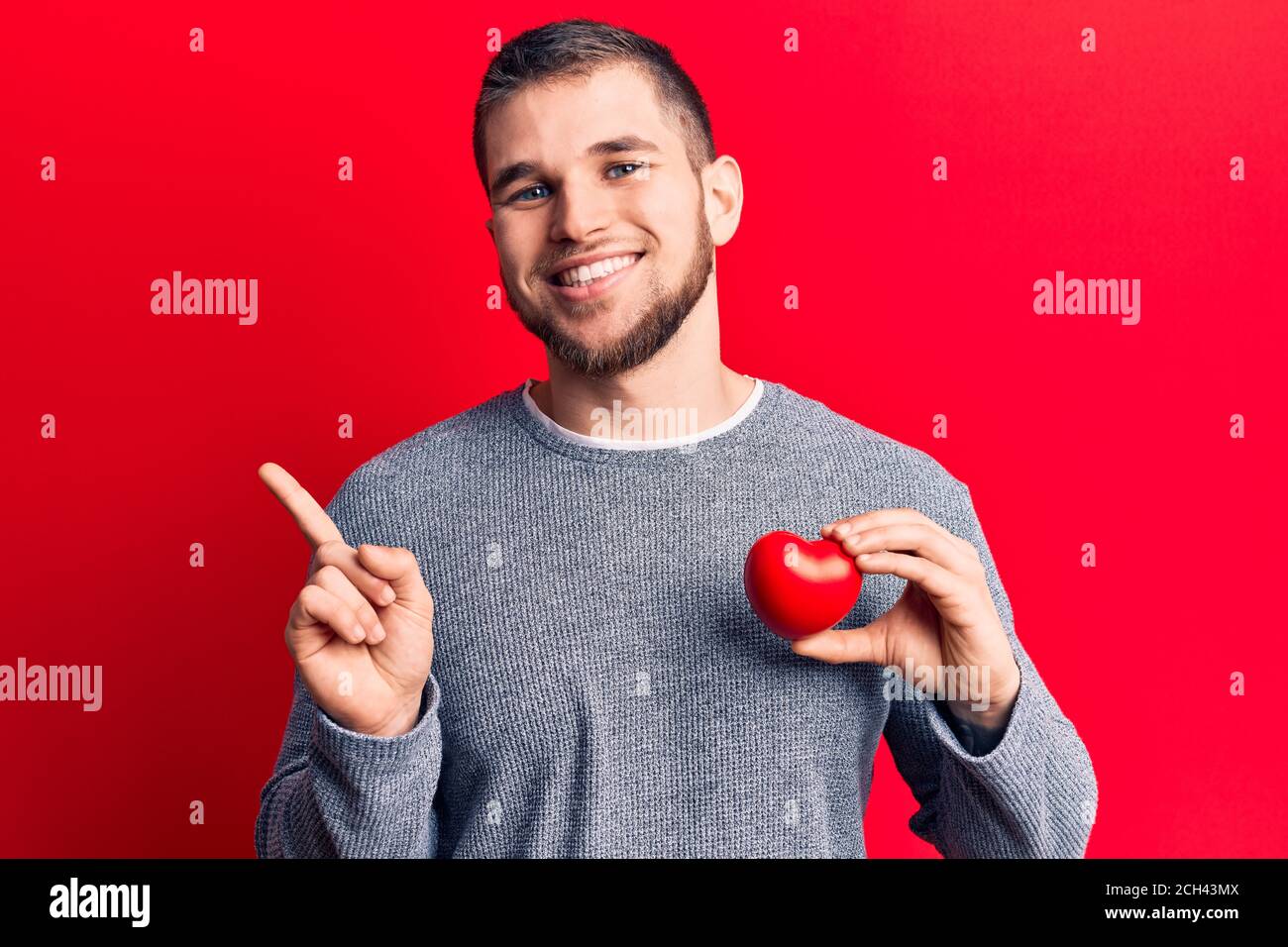 Young handsome man holding heart smiling happy pointing with hand and ...