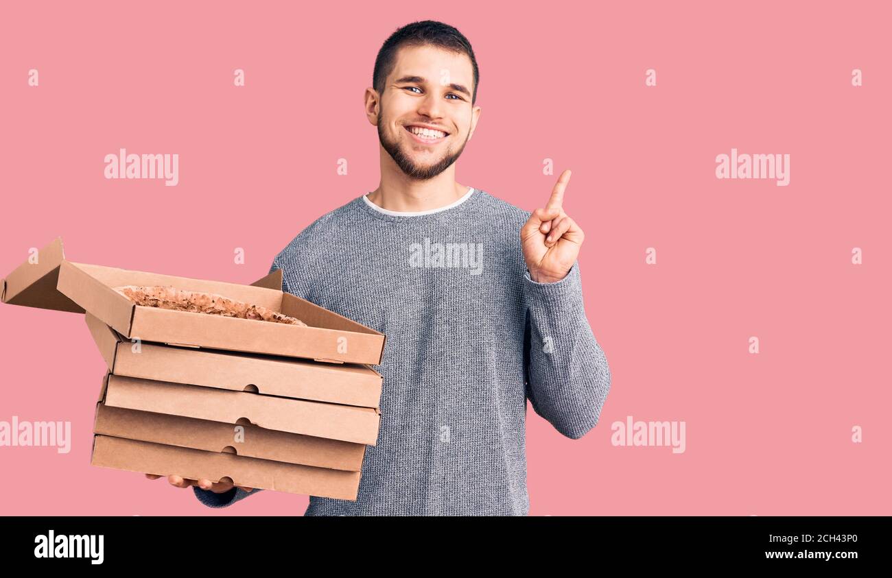 Young handsome man holding delivery italian pizza boxes surprised with ...
