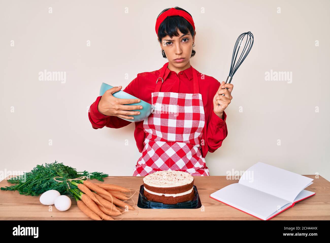 Beautiful brunettte woman cooking carrot cake using whisk skeptic and ...