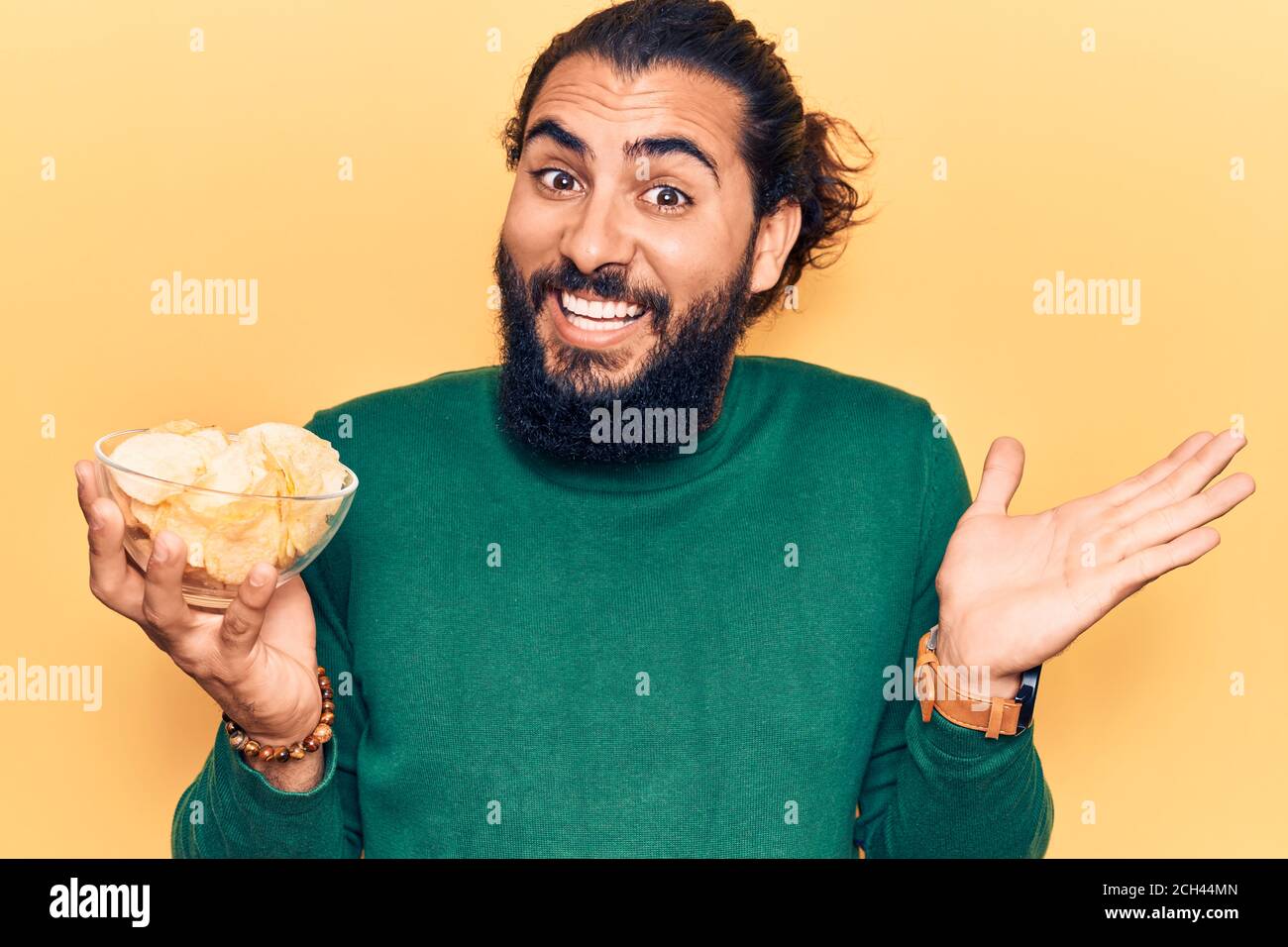 Young arab man holding potato chip celebrating achievement with happy ...