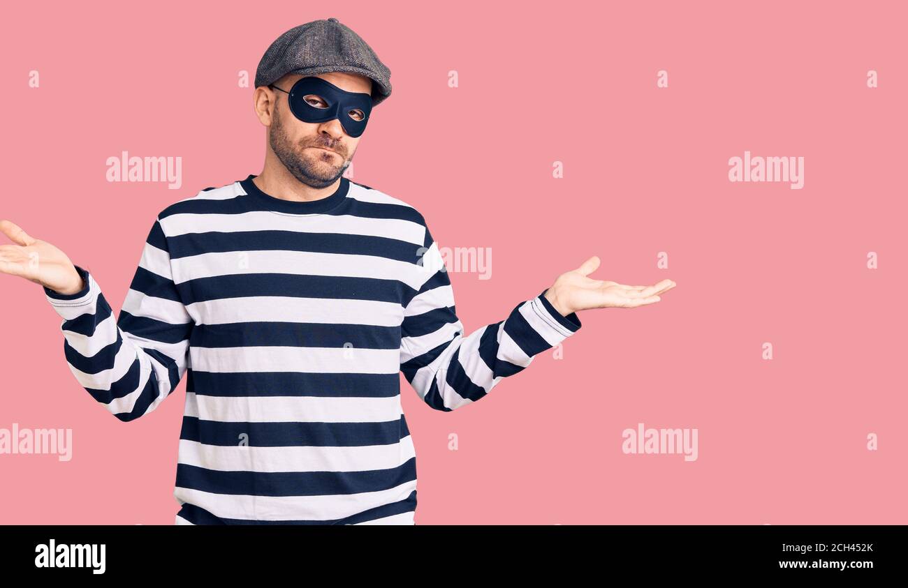 Young handsome man wearing burglar mask clueless and confused ...