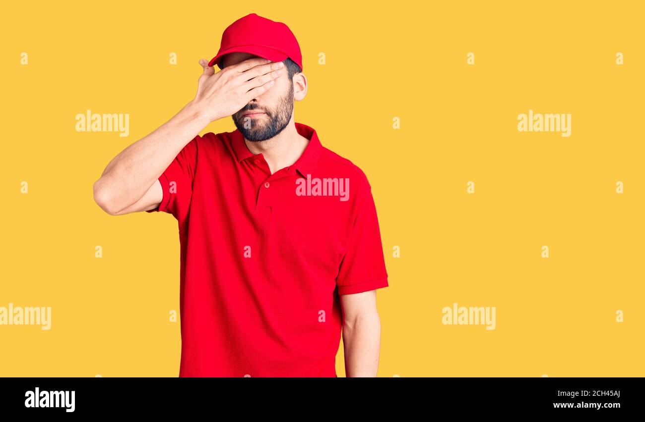 Young Handsome Man With Beard Wearing Delivery Uniform Covering Eyes