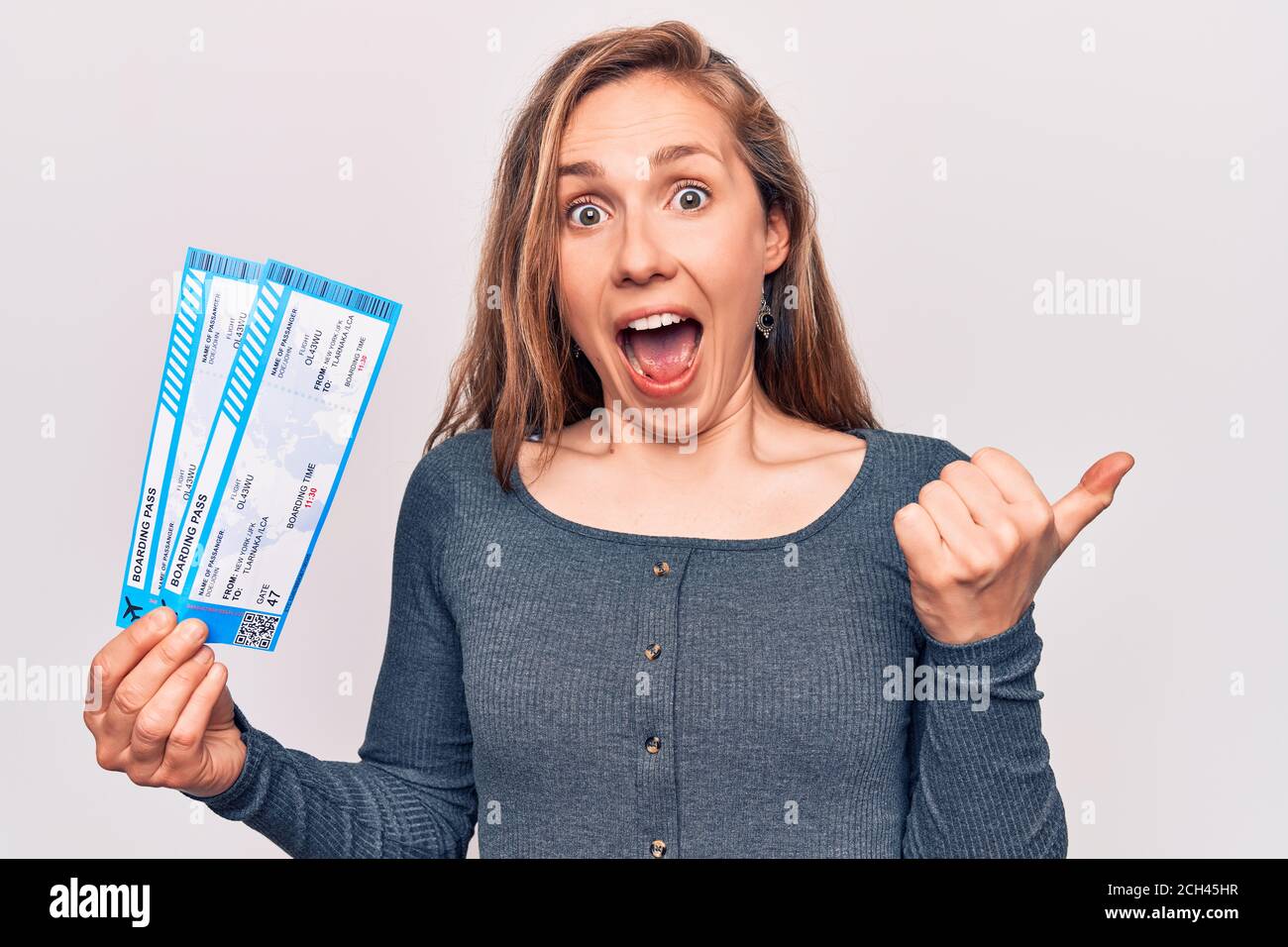 Young beautiful blonde woman holding boarding pass pointing thumb up to ...