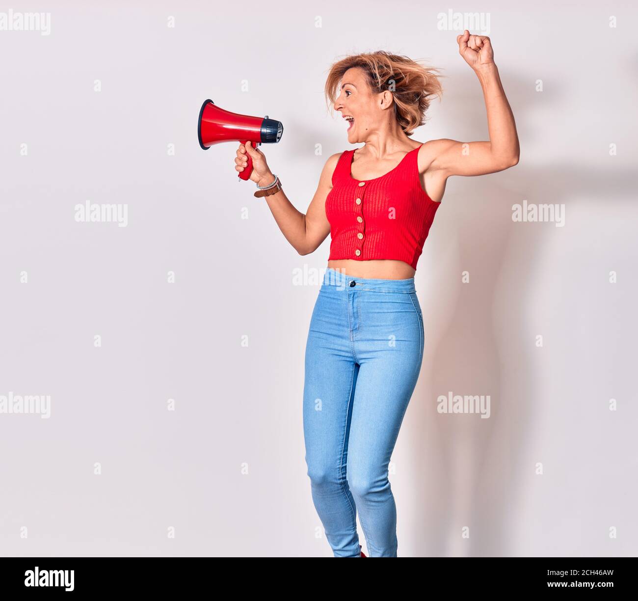 Young beautiful caucasian woman screaming using megaphone. Jumping over ...