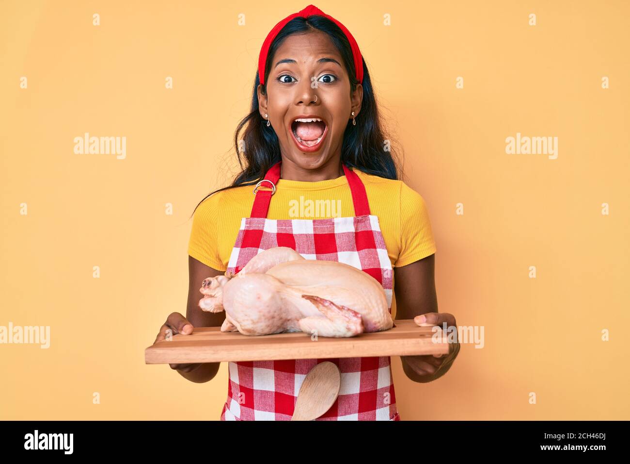 Young indian girl wearing cook apron and holding chicken celebrating ...