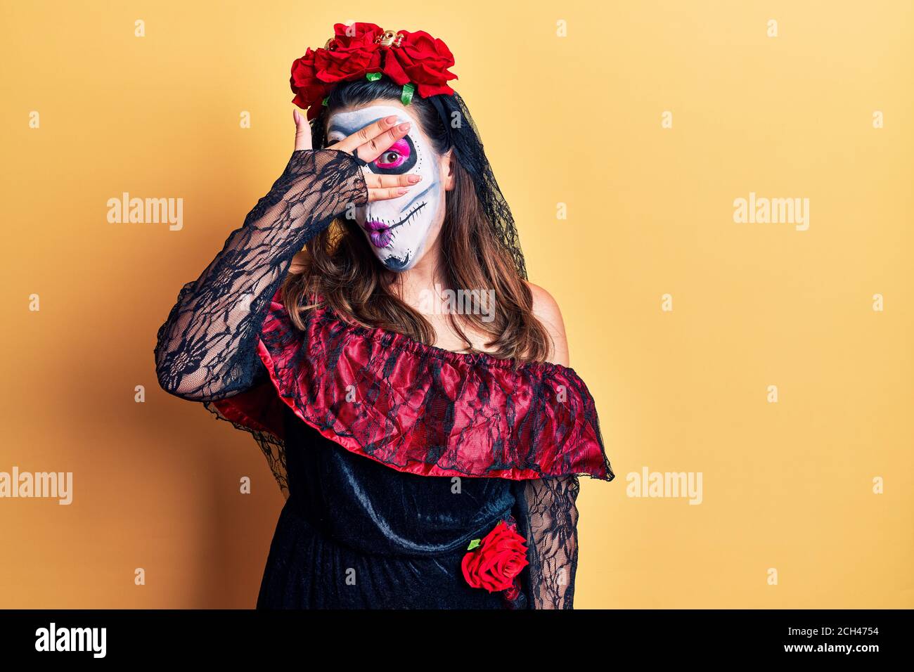 Young woman wearing day of the dead costume over yellow peeking in ...