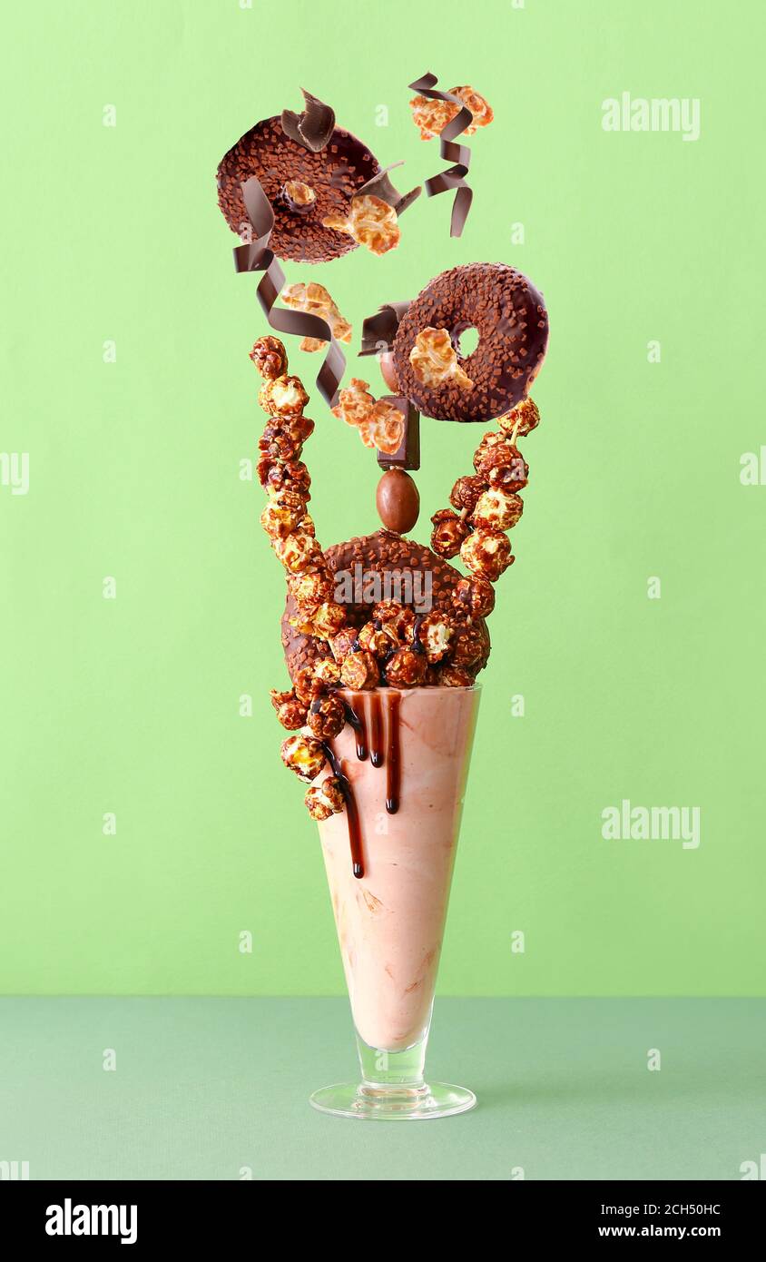 Glass of delicious freak shake and falling ingredients on color ...
