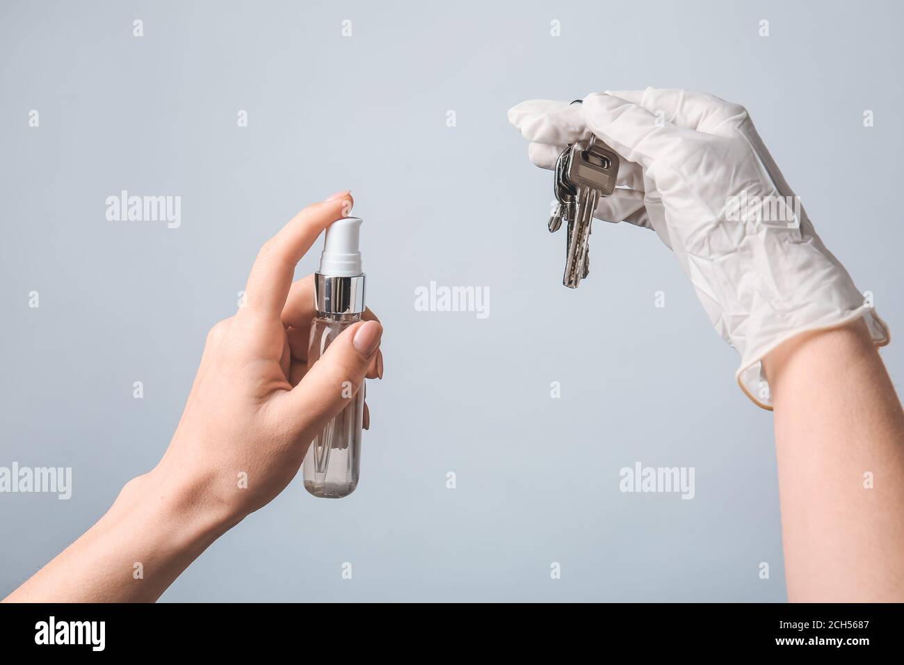 Woman disinfecting keys from house on grey background Stock Photo - Alamy