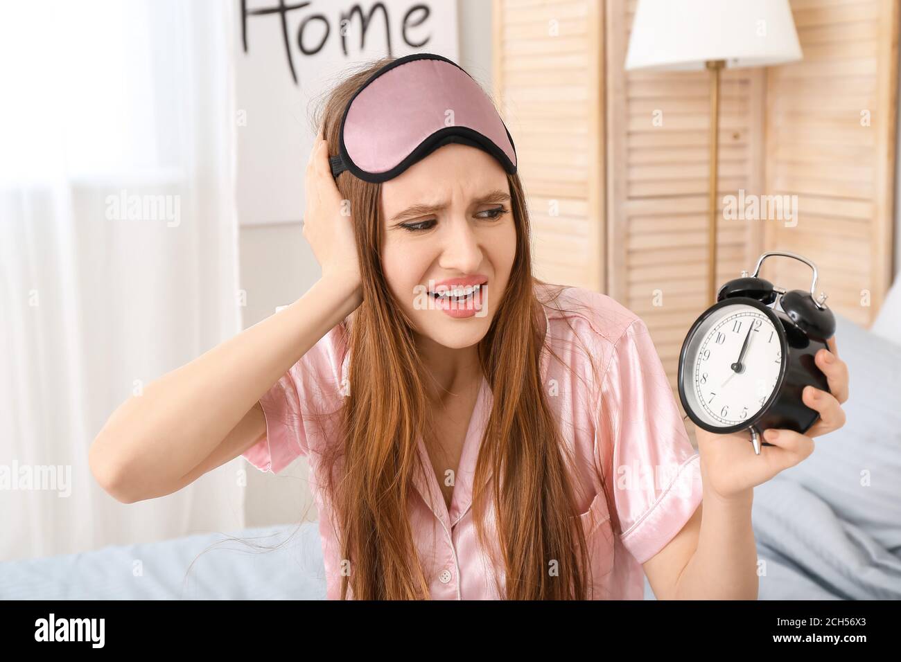 Stressed woman with alarm clock suffering from insomnia in bedroom ...