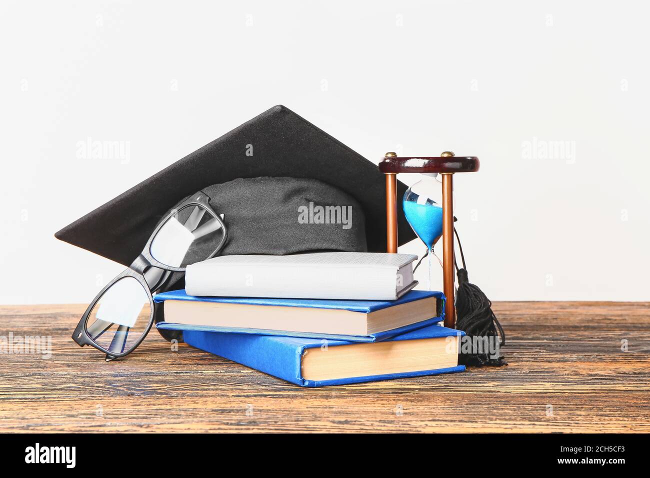 Graduation hat, books and hourglass on table against white background ...