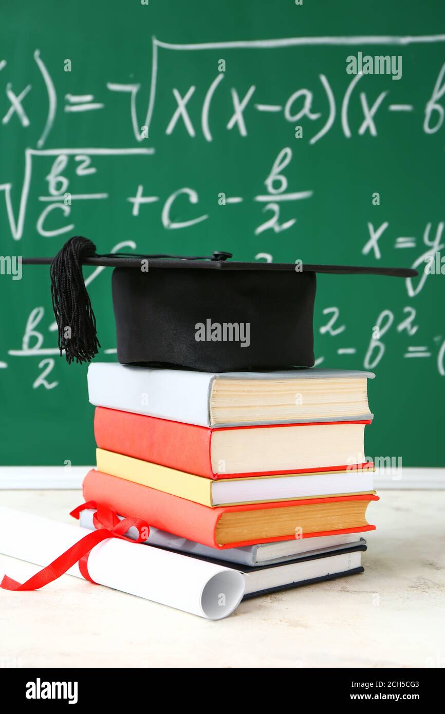 Graduation hat, books and diploma on table in classroom Stock Photo - Alamy