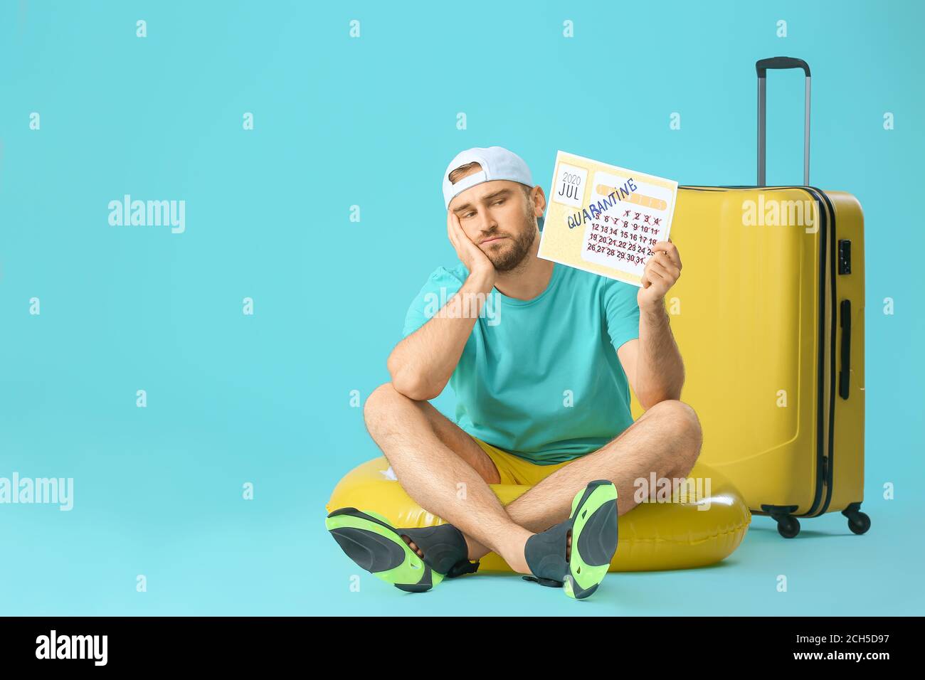 Sad man holding calendar with written word QUARANTINE and suitcase ...