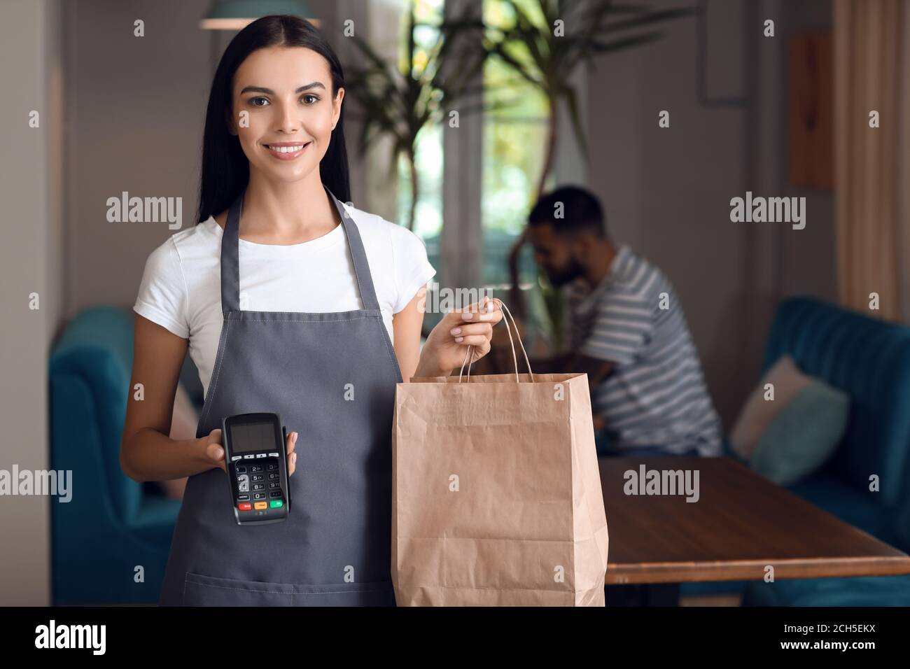 Young waitress with food for delivery and payment terminal in ...