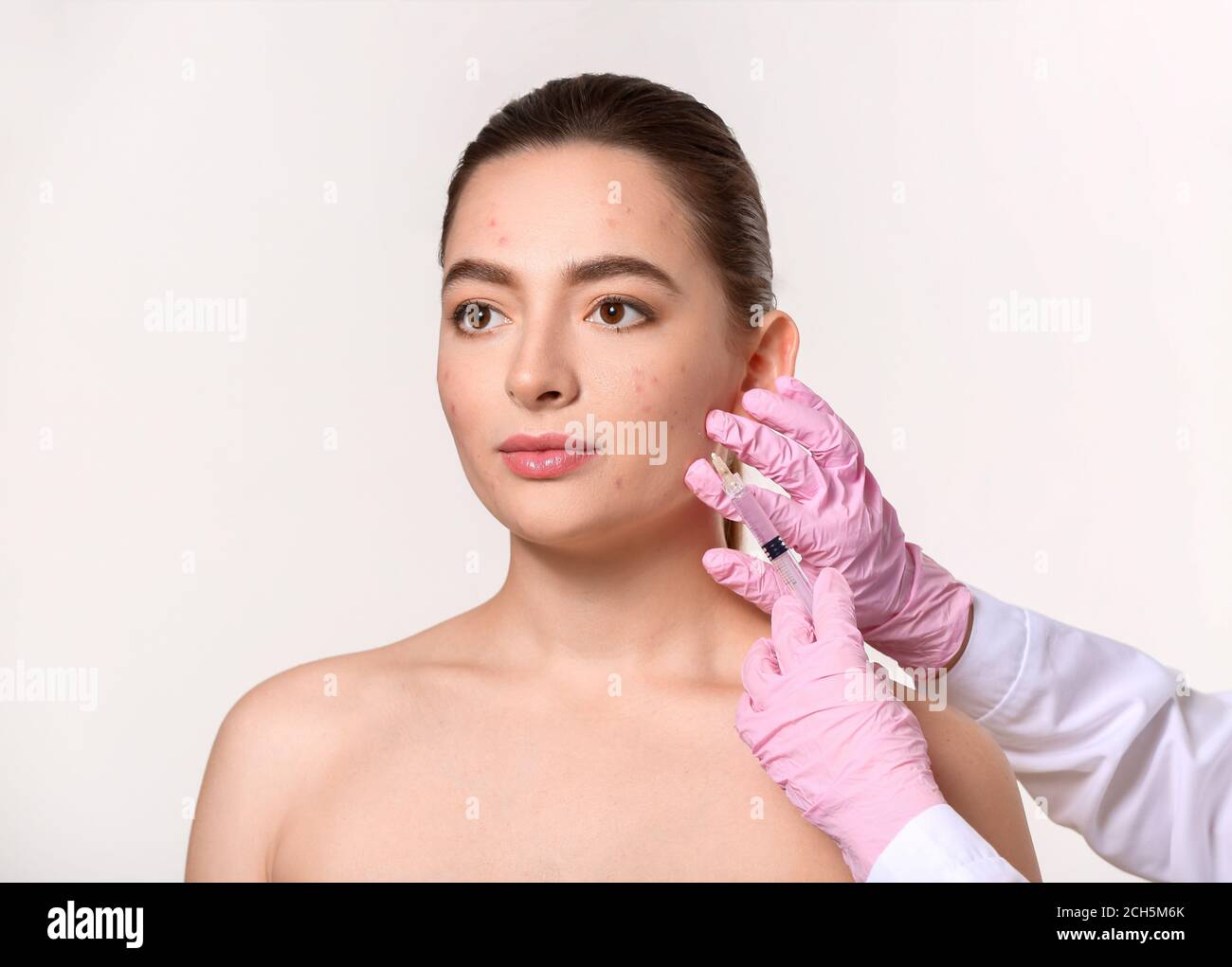 Young woman with acne problem receiving injection in her face against ...
