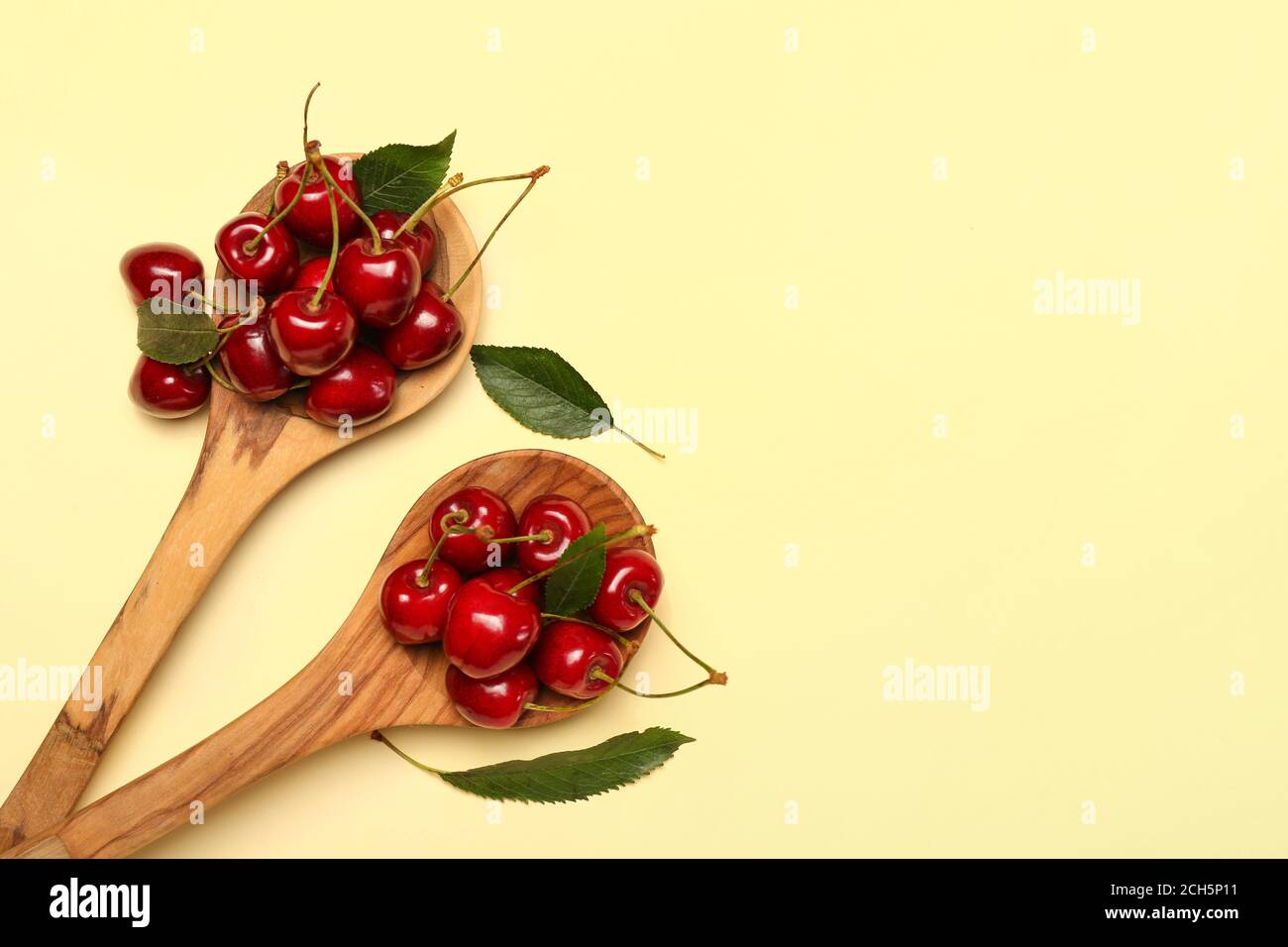 Spoons with sweet cherry on color background Stock Photo - Alamy