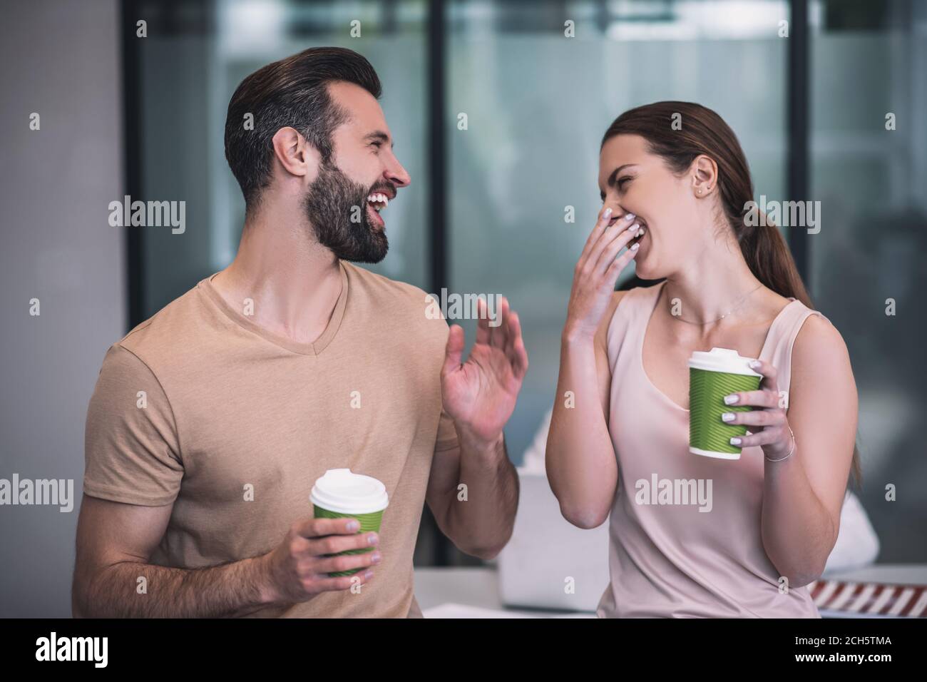 Bearded male and brown-haired female coworkers enjoying coffee ...