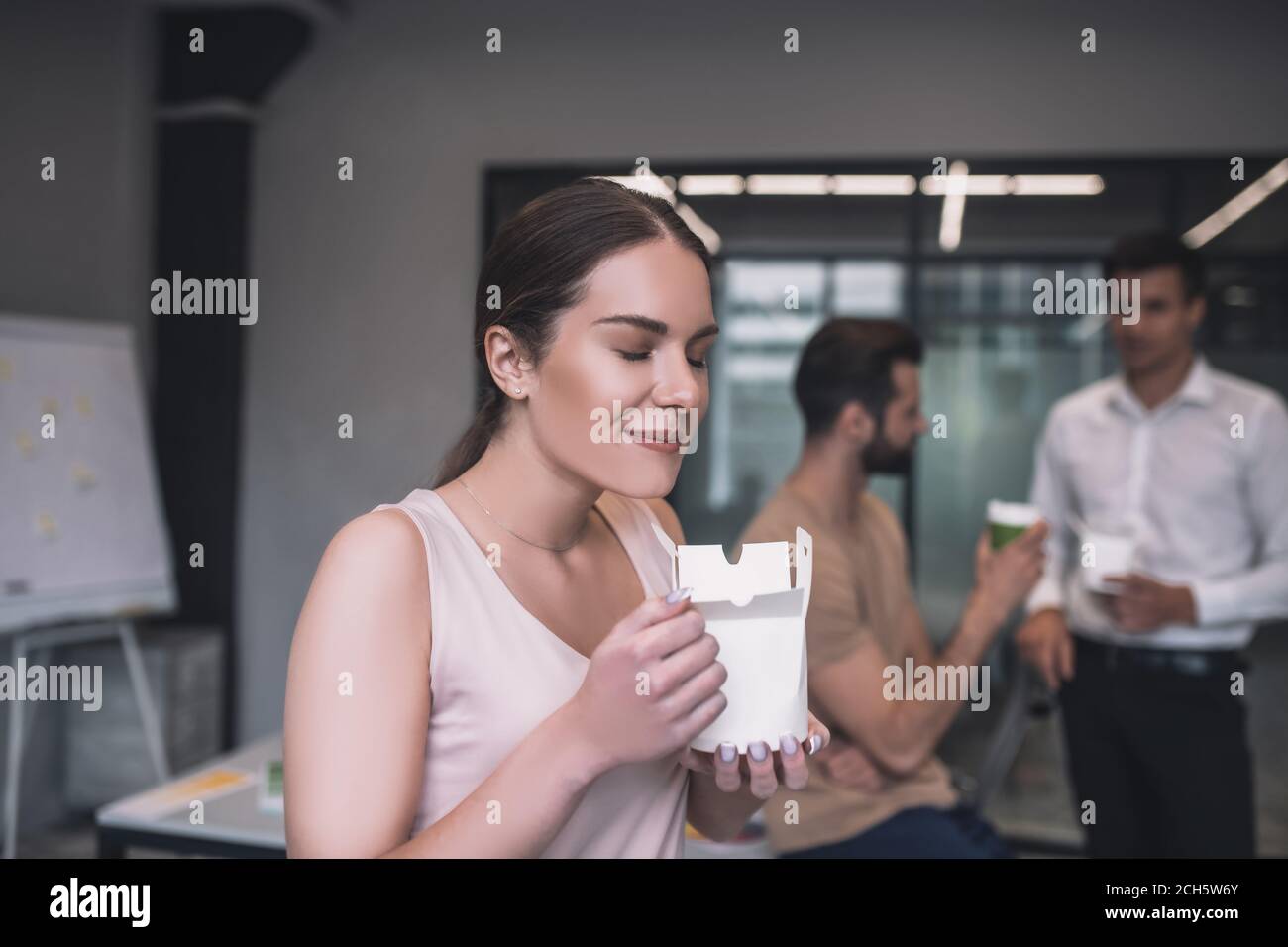 Dark-haired female smelling chinese food box, her male colleagues ...