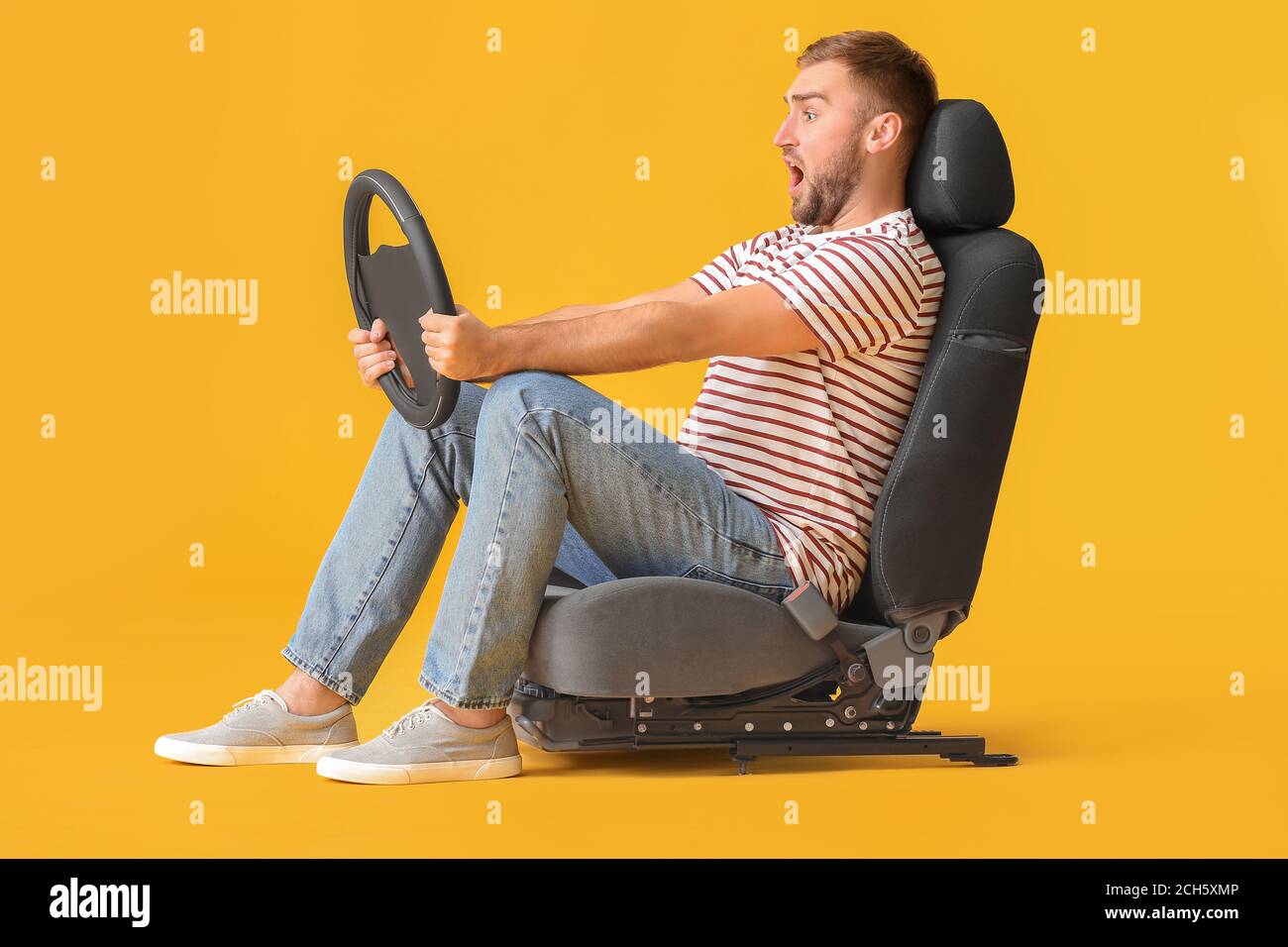 Surprised man with steering wheel sitting on car seat against color ...