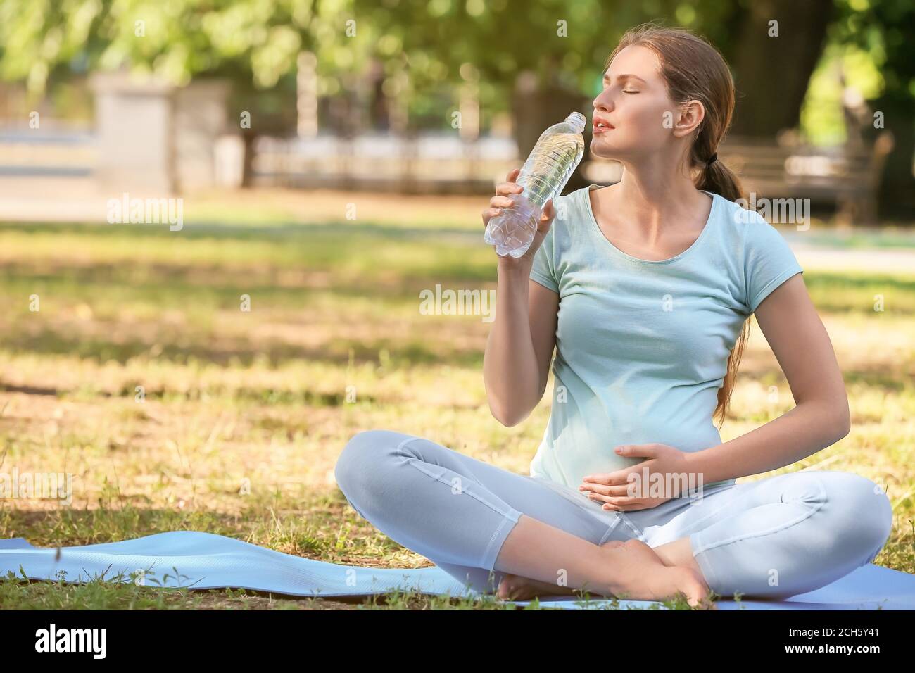 Young pregnant woman drinking water while practicing yoga outdoors ...