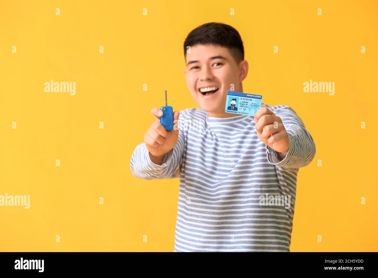 Happy Asian man with car key and driving license on color background ...