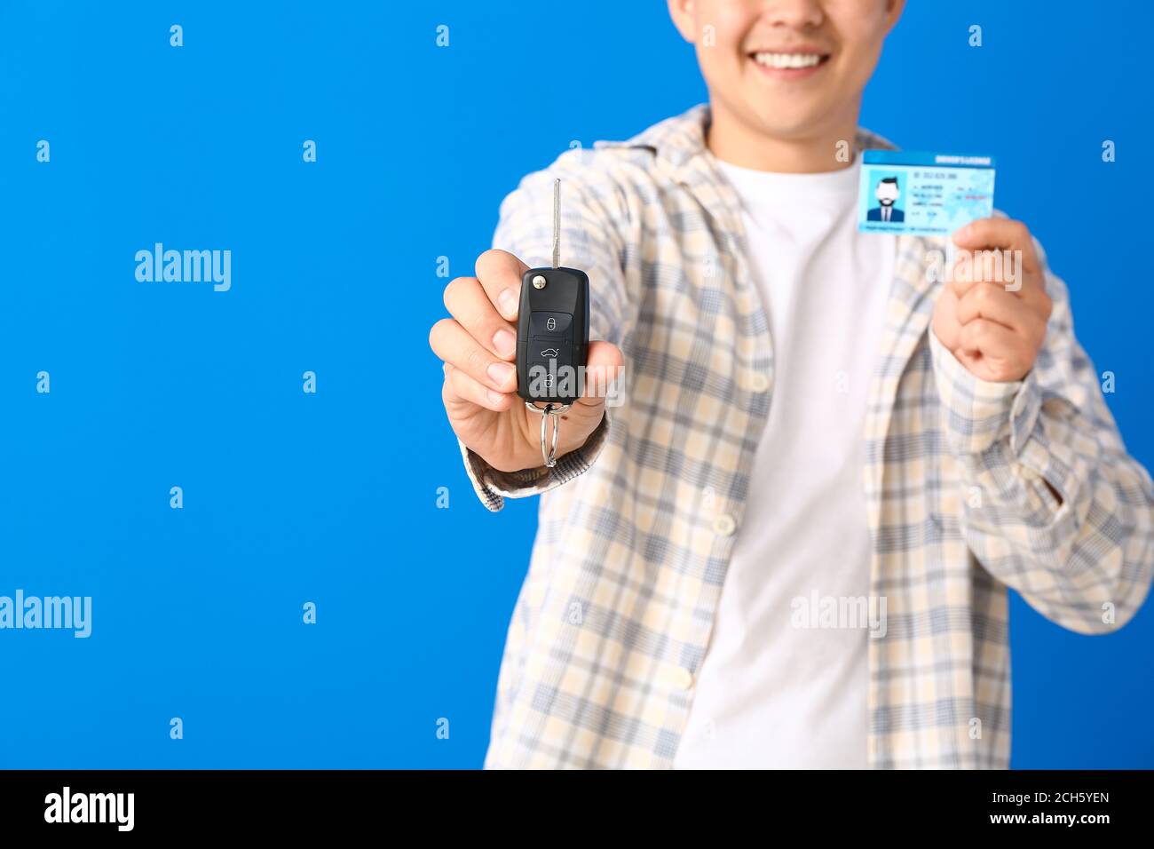 Happy Asian man with car key and driving license on color background ...