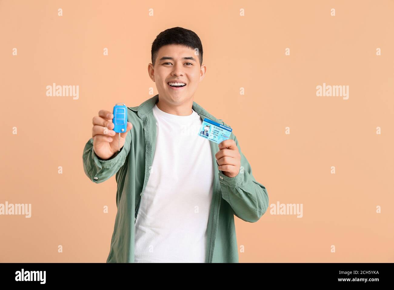 Happy Asian man with car key and driving license on color background ...