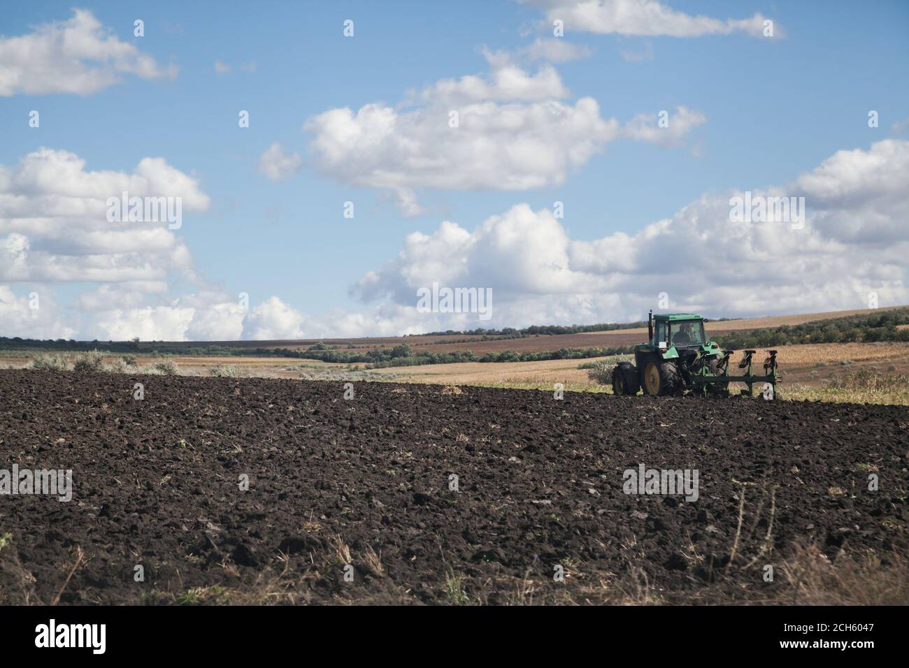 Tractor plowing black soil field with blue sky and white clouds Stock ...