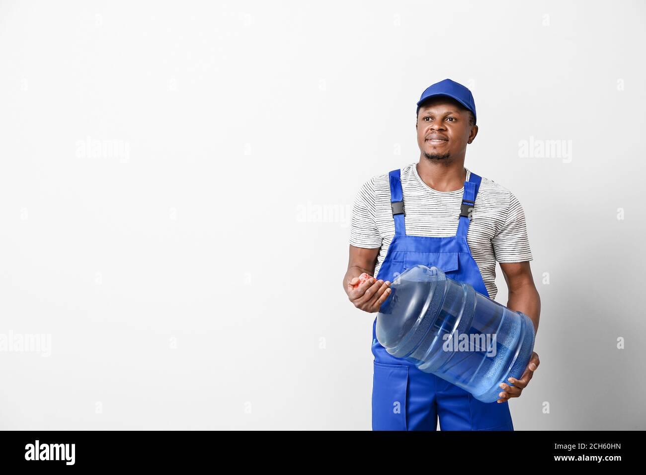 African-American delivery man with bottle of water on light background ...
