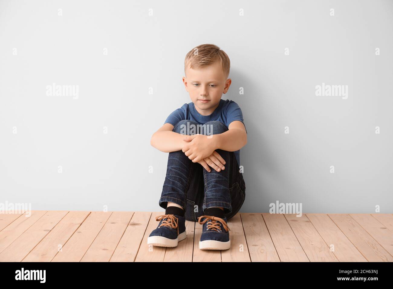 Sad little boy with autistic disorder sitting near light wall Stock ...