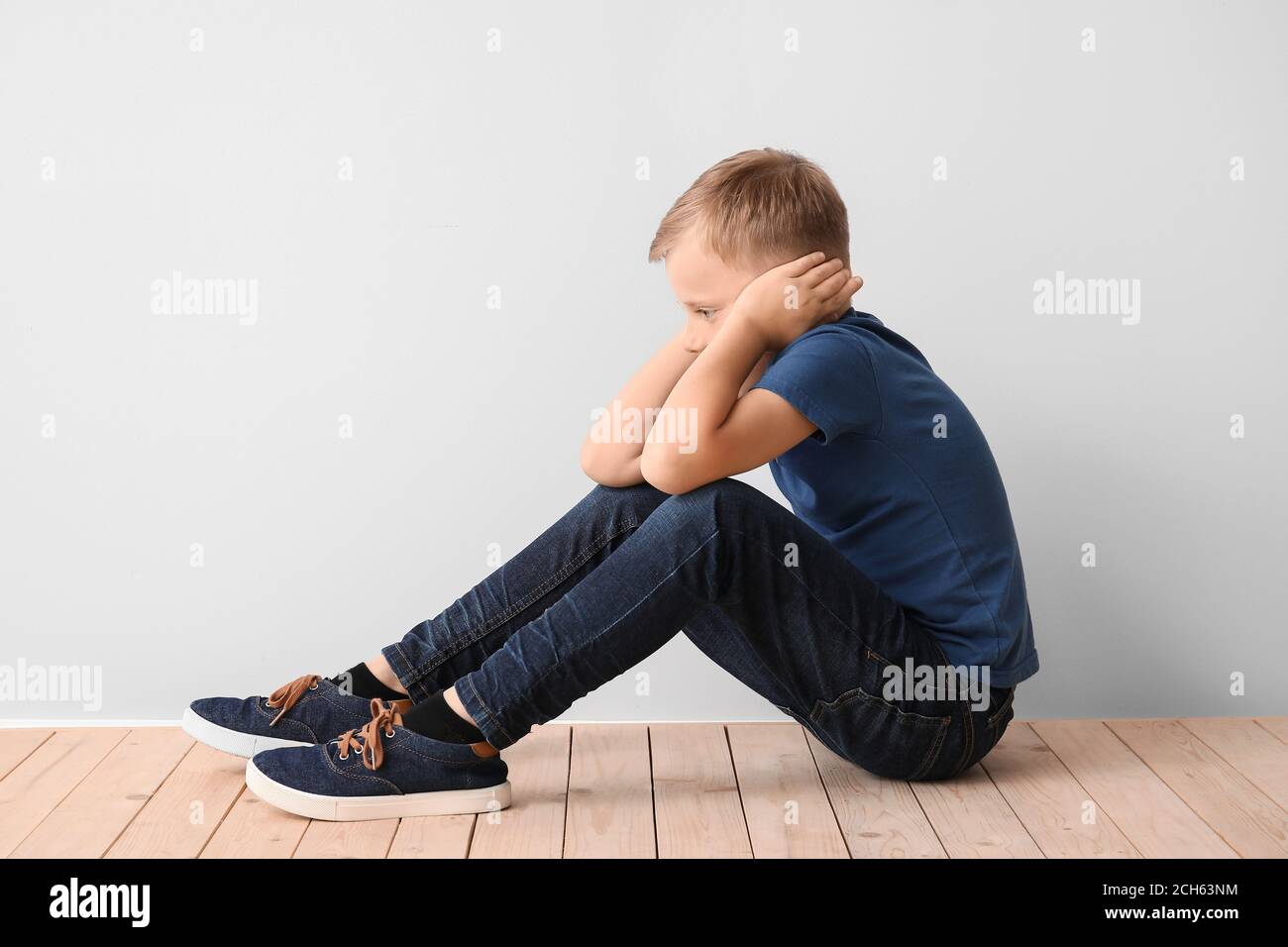 Sad little boy with autistic disorder sitting near light wall Stock ...