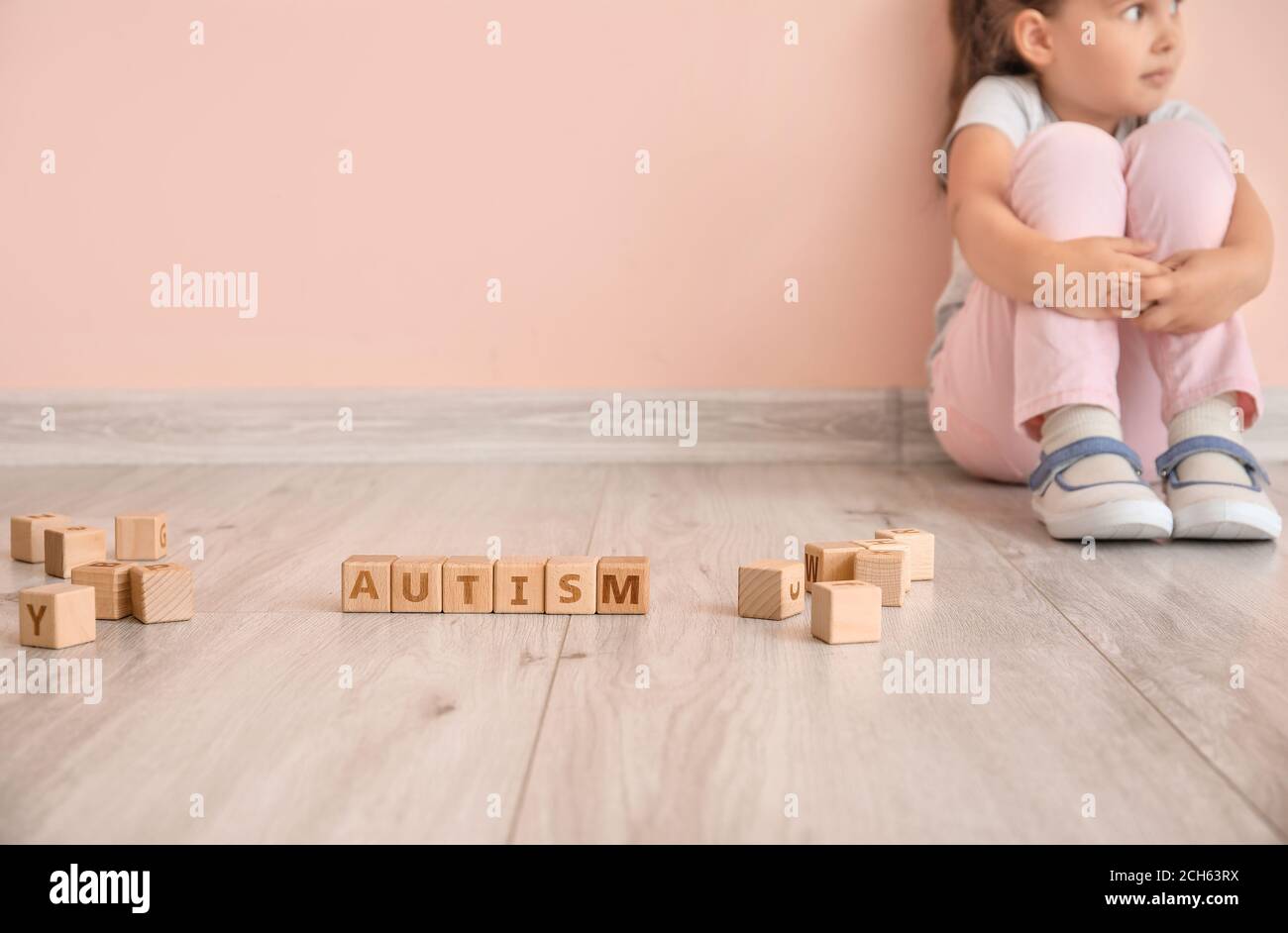 Little girl with autistic disorder and cubes sitting near color wall ...
