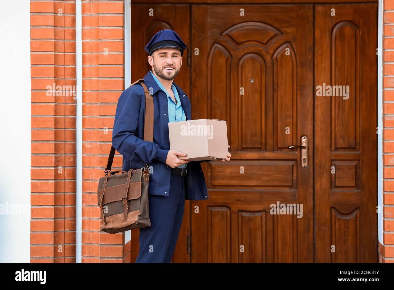 Handsome young postman with parcel outdoors Stock Photo - Alamy