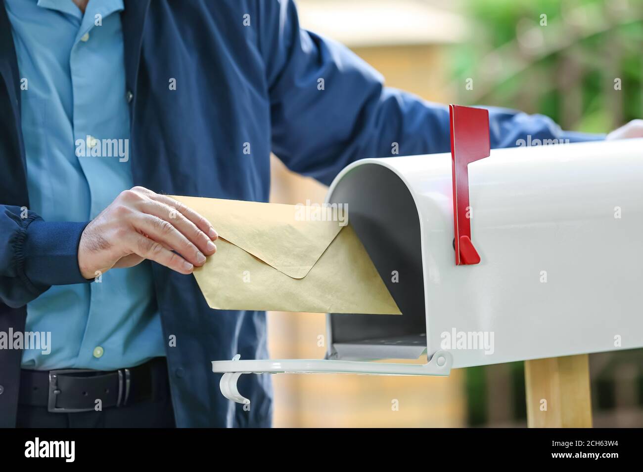 Handsome young postman putting letter in mail box outdoors Stock Photo ...